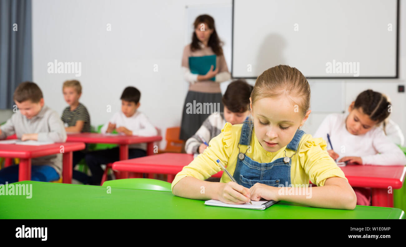 Portrait of little assiduous girl with pen and notebook at lesson in ...