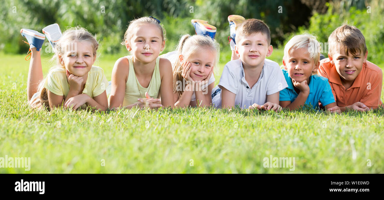 portrait of smiling european children lying on grass in park and ...