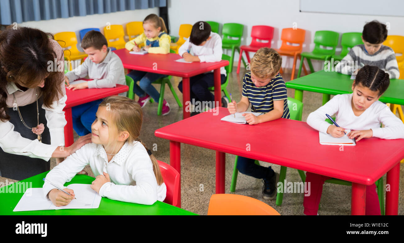 Friendly teacher woman helping children during lesson in schoolroom ...