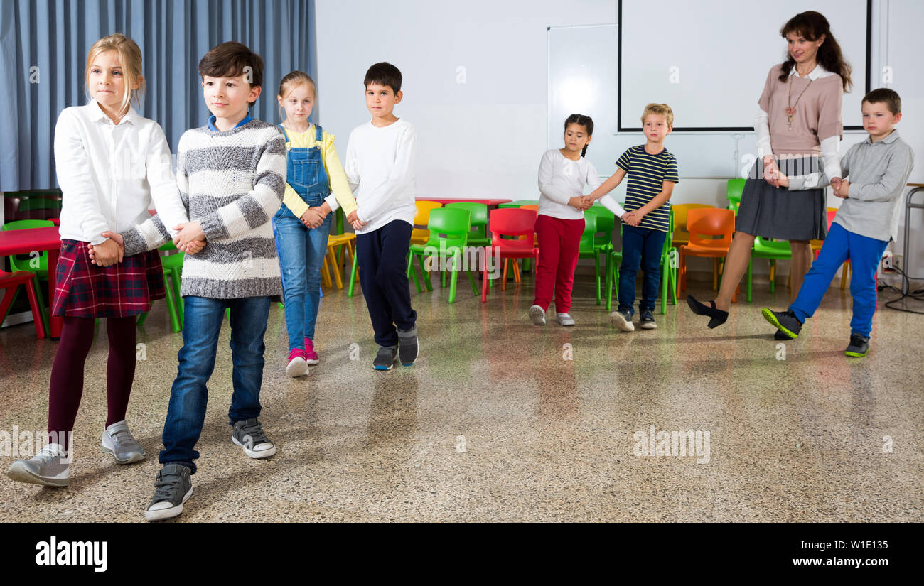 Group of cheerful school kids learning to dance in pairs with their ...