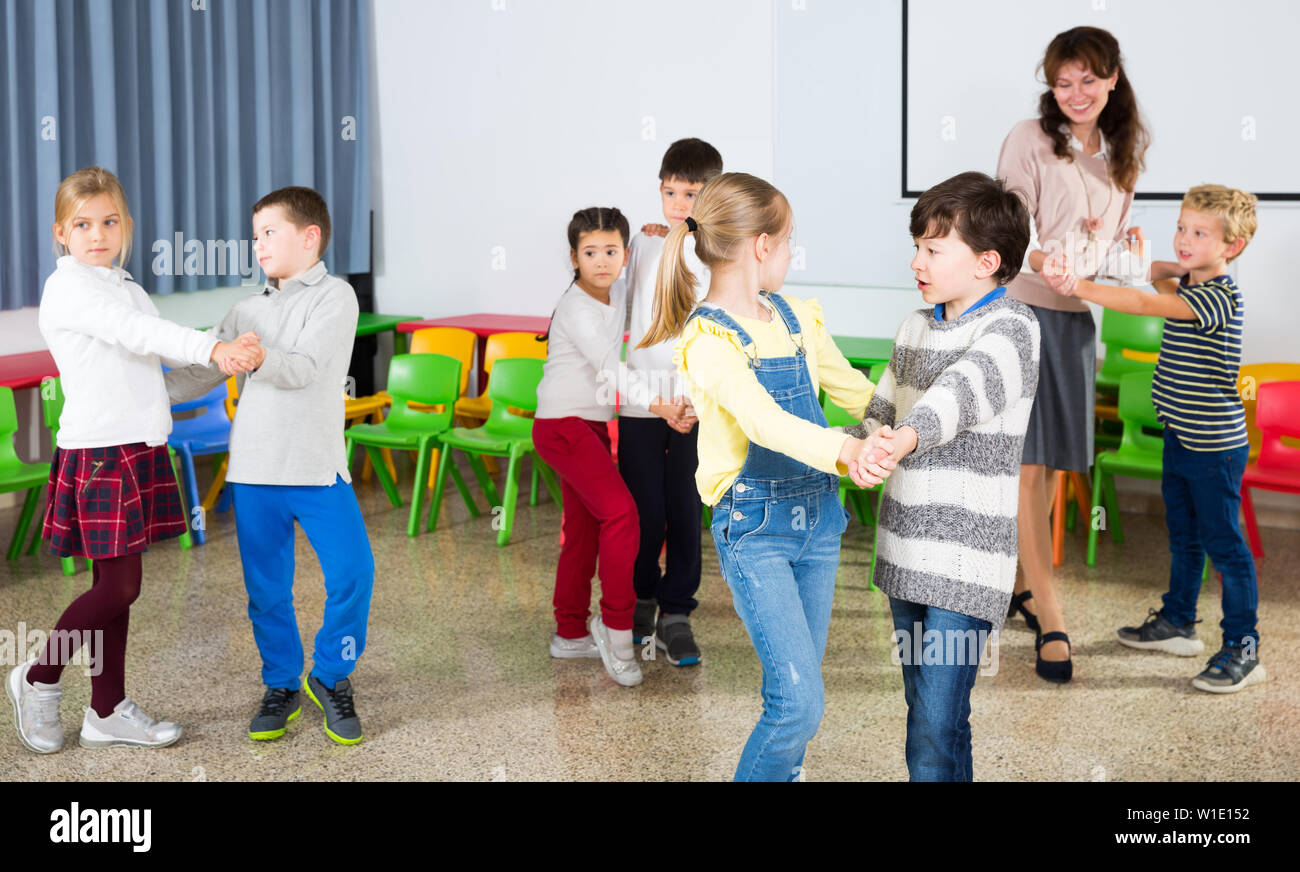 Group of cheerful school kids learning to dance in pairs with their ...