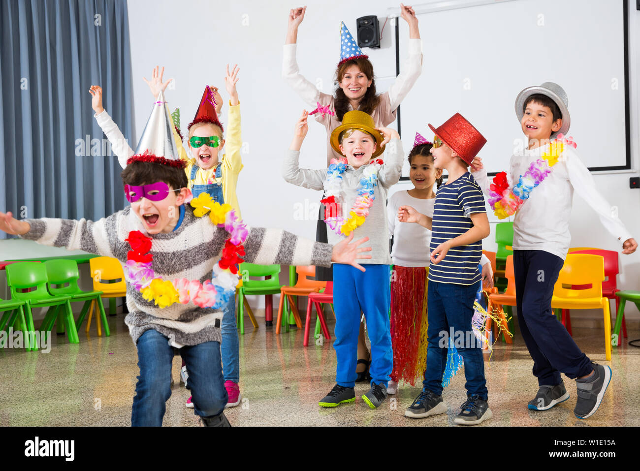 Cheerful pupils and female teacher with funny hats and festive ...