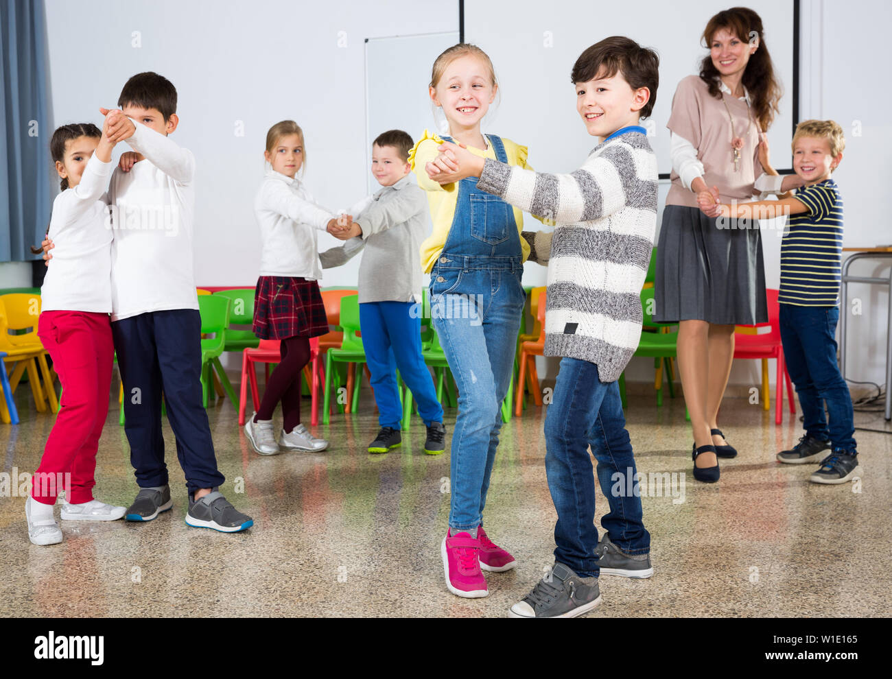 Happy kids and female teacher dancing together in classroom at ...
