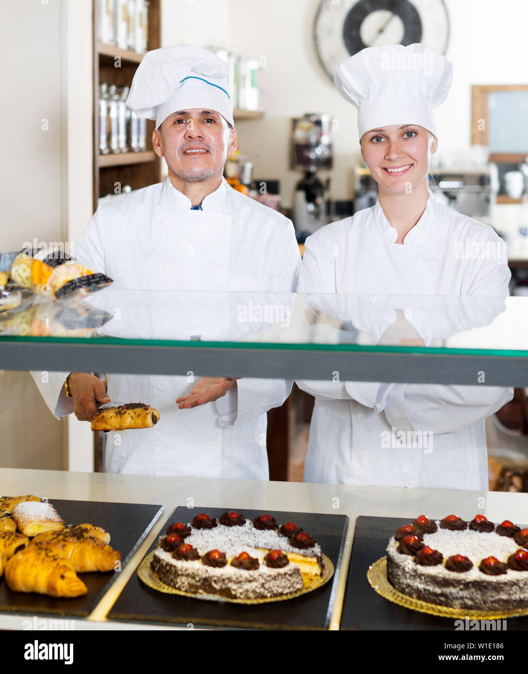 Smiling experienced man and woman staff offering cakes and buns in ...
