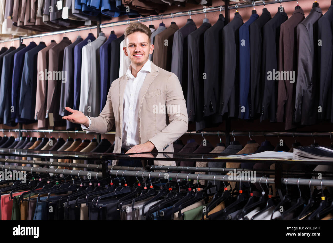 happy russian male shopping assistant offering various suits in men’s ...