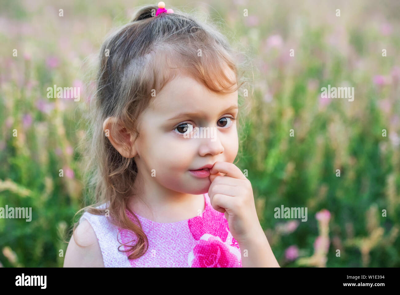 Cute serious baby girl looks aside outdoors in green field. Child ...
