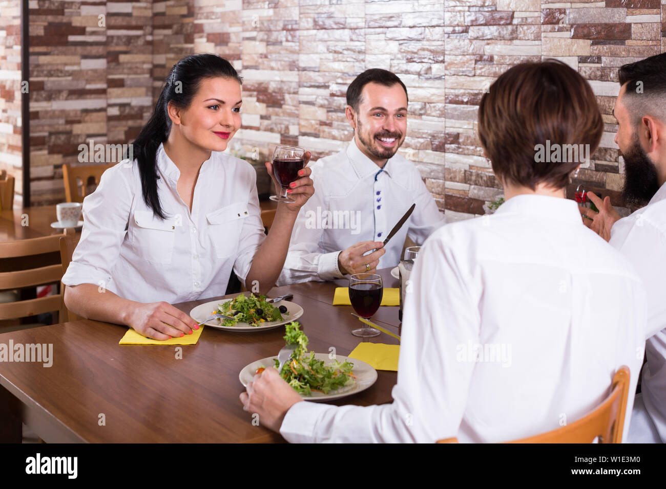 group of satisfied friends eating at restaurant table and chatting ...