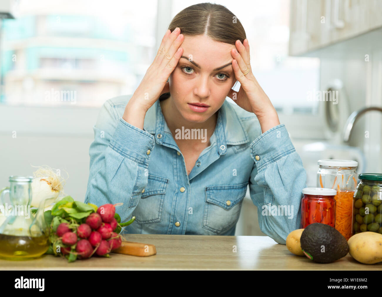 Depressed and sad young housewife sitting in kitchen. Tiredness and ...