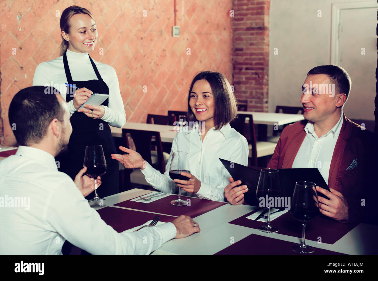 Cheerful female waiter writing down order from visitors in country ...