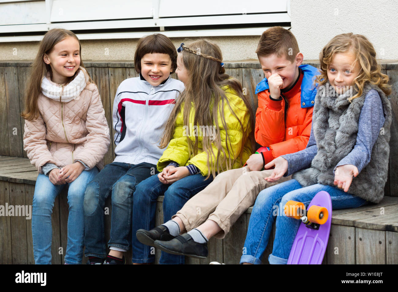 Group of happy positive children sitting on bench and sharing secrets ...