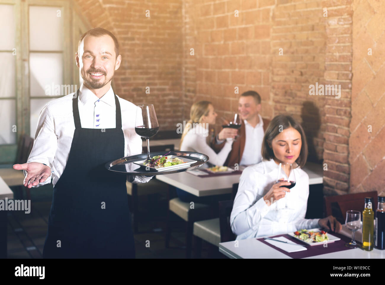 Glad male waiter showing country restaurant to visitors Stock Photo - Alamy