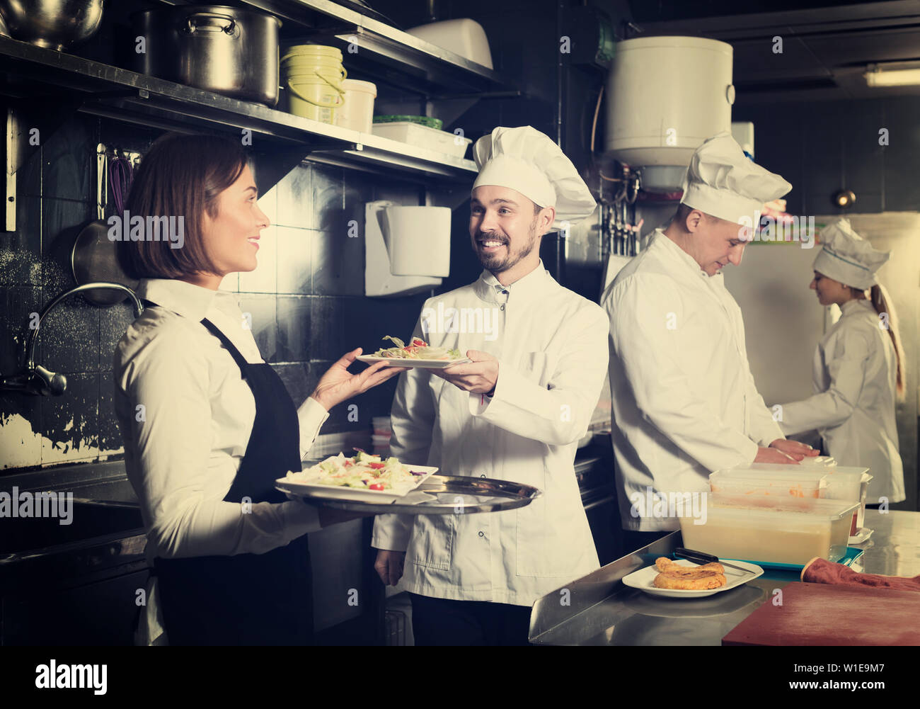 Smiling female waiter taking order of meal from restaurant’s kitchen ...