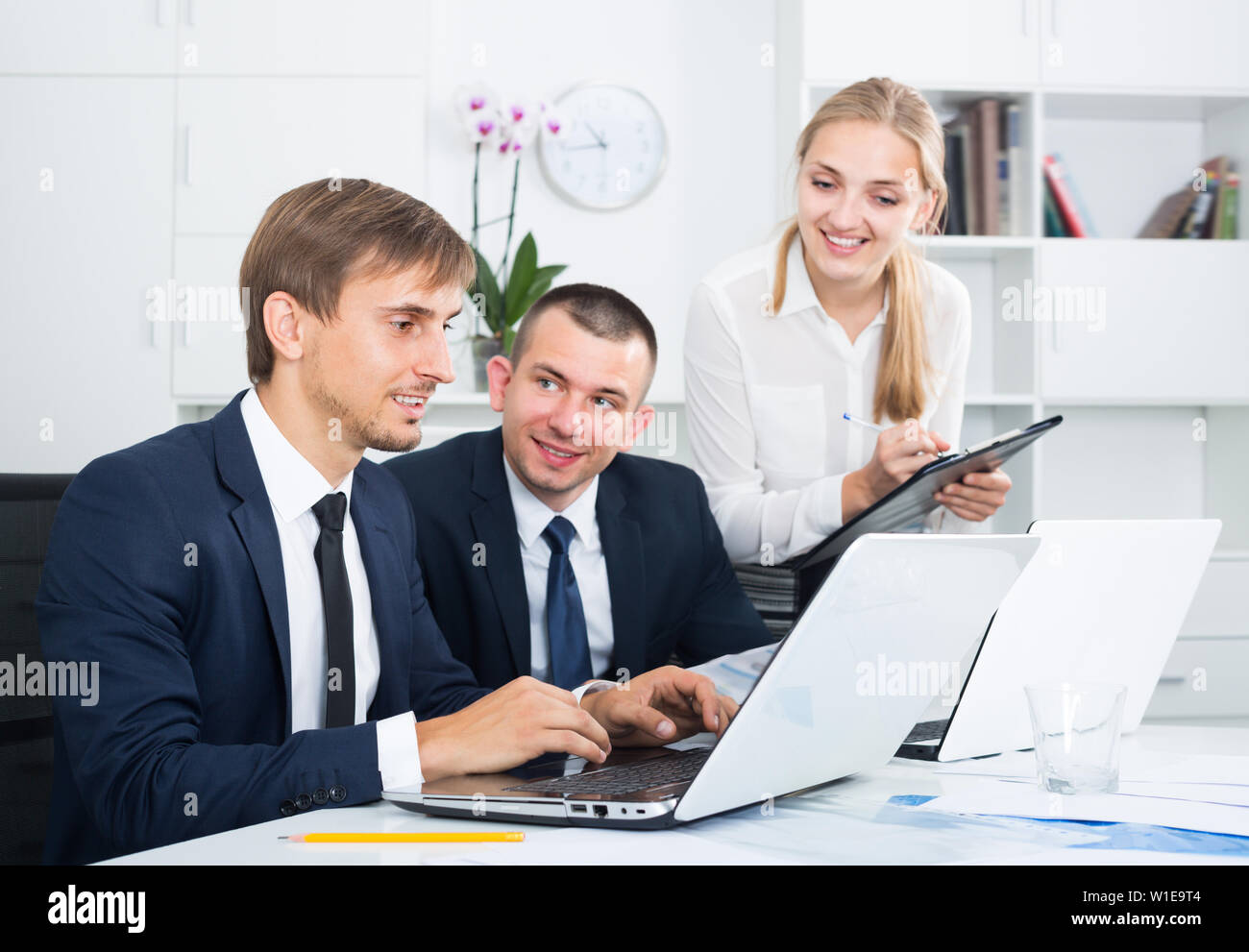 Two glad business male assistants working using laptops and woman with ...
