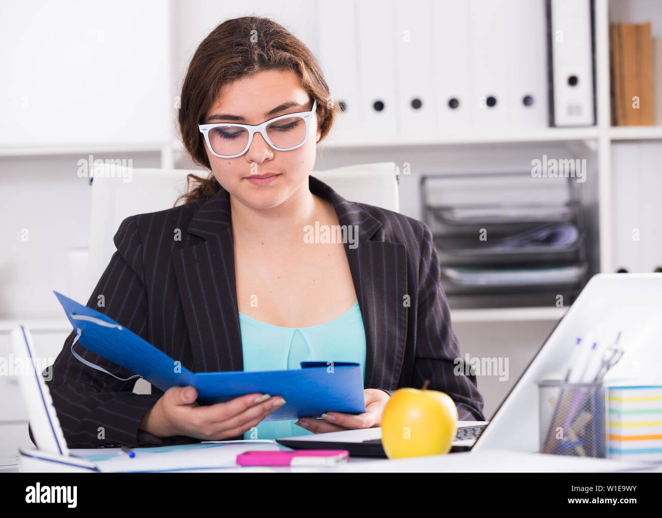 Female office worker is reading documents before signing it in office ...