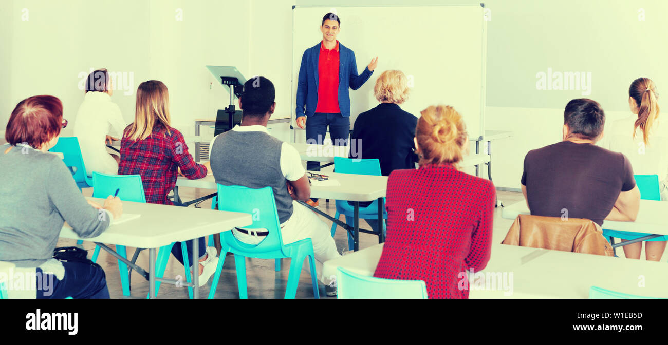Friendly male teacher lecturing to attentive adult students at ...
