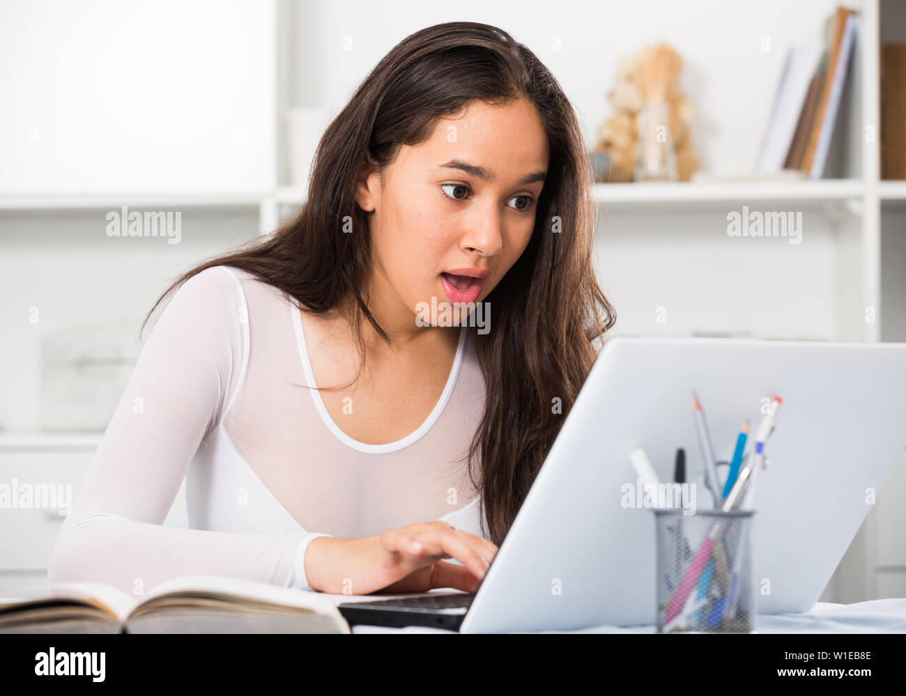 Young girl reading info in laptop and surprised indoors Stock Photo - Alamy