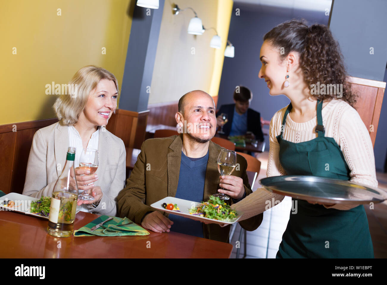 Friendly smiling waitress serving elderly couple at dinner in cafe ...