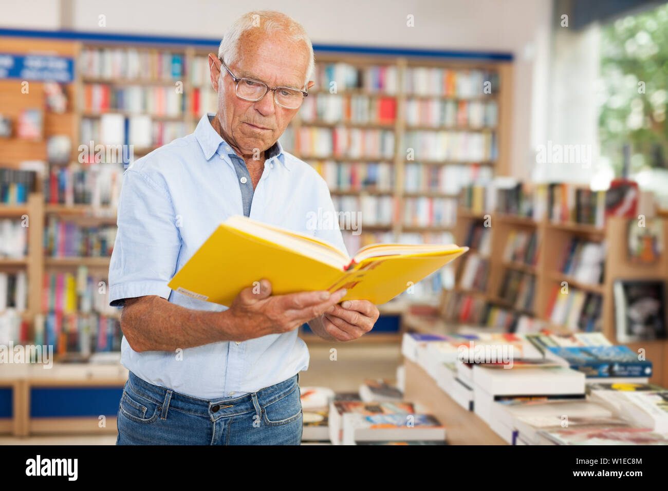 Portrait of focused older man looking inside of books while visiting ...