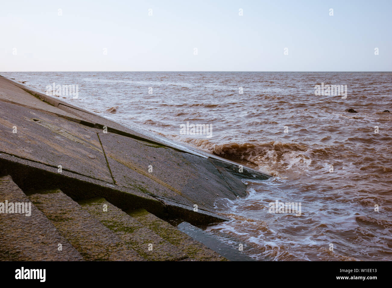 Sea water and waves hitting a sloping concrete revetment or seawall as ...