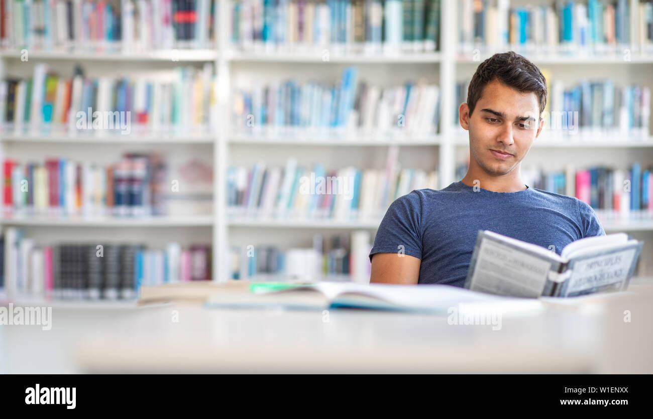 Students in a library - handsome student reading a book for his class in a bright modern library ...