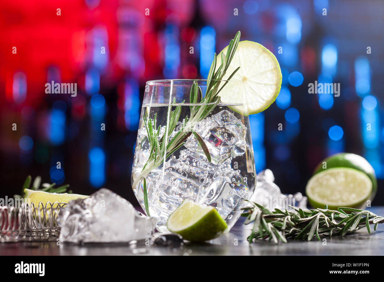 Glass with alcoholic drink with lime, ice and rosemary on bar lights ...
