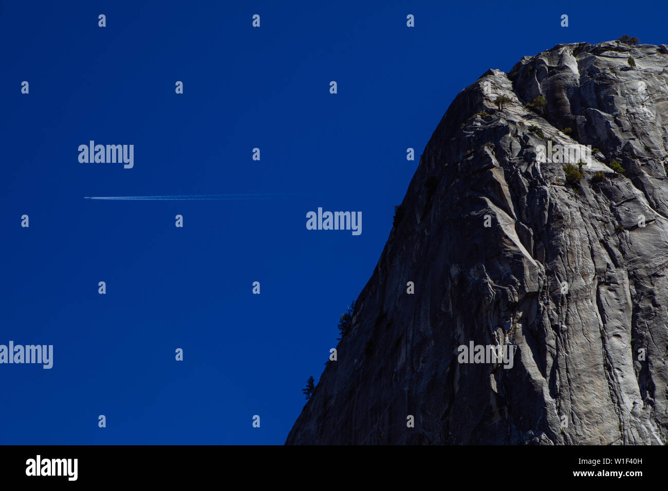 Airplane on a plain blue sky leaving a trail with Liberty Cap rock ...