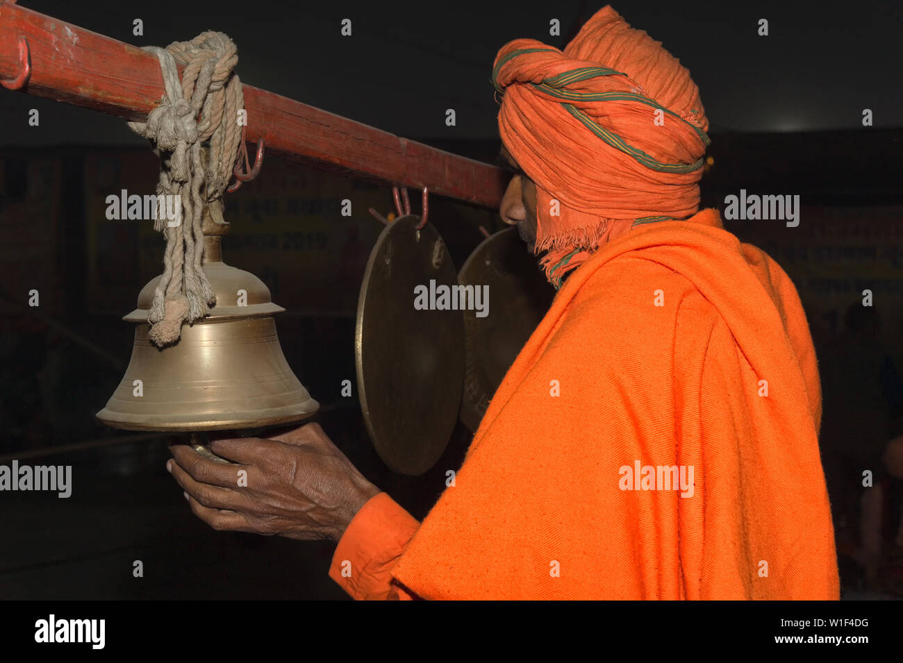 Hindu priest in saffron cloth ringing the bell at night, Allahabad ...