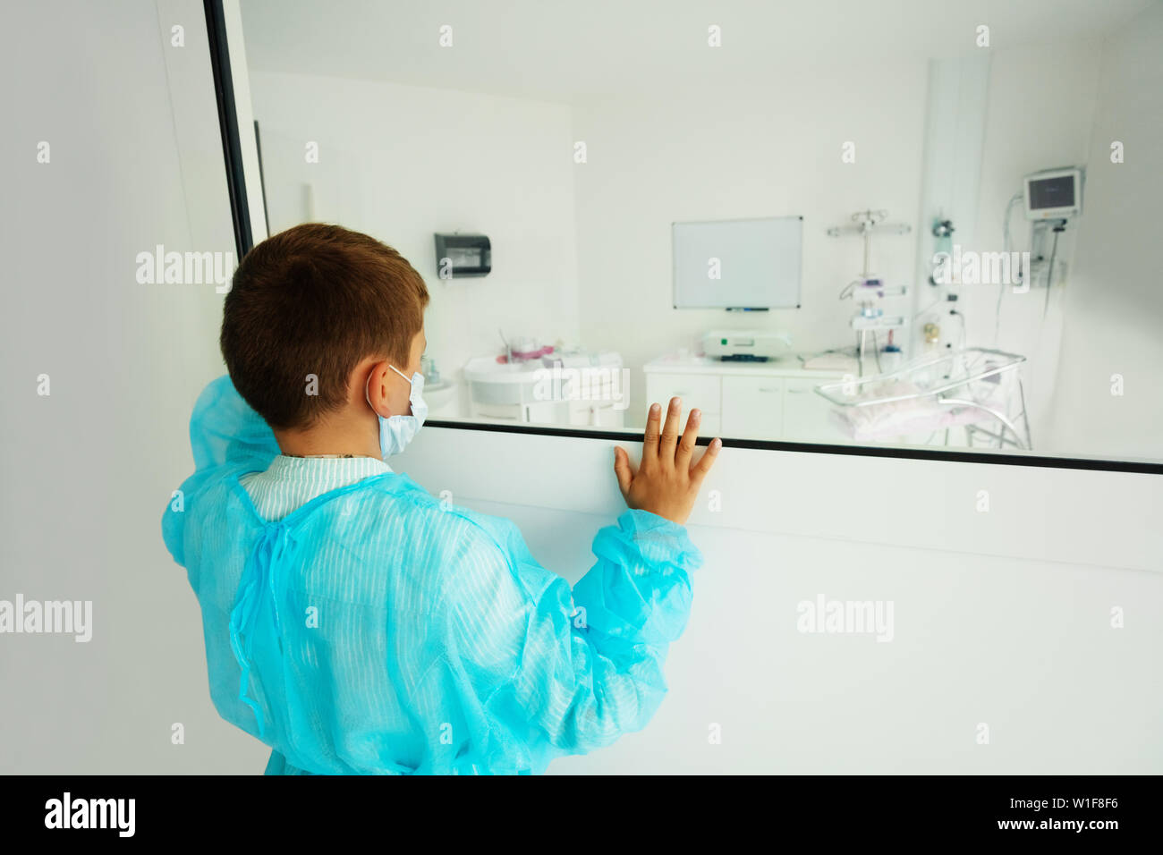 Little boy near the window of ICU room in hospital wearing medical mask ...
