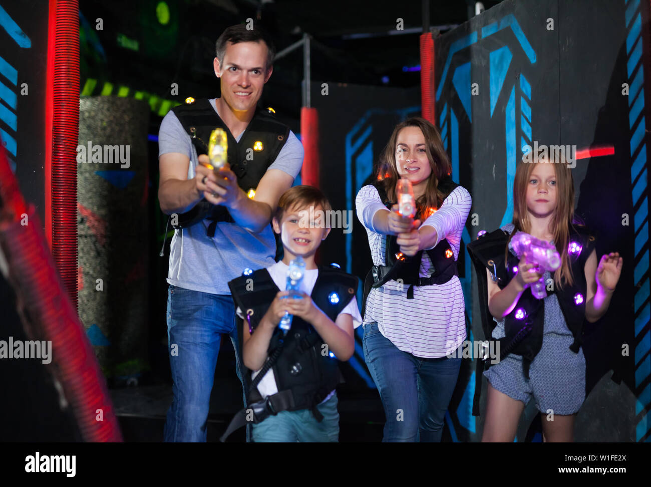 Modern young parents and children with laser pistols playing laser tag ...