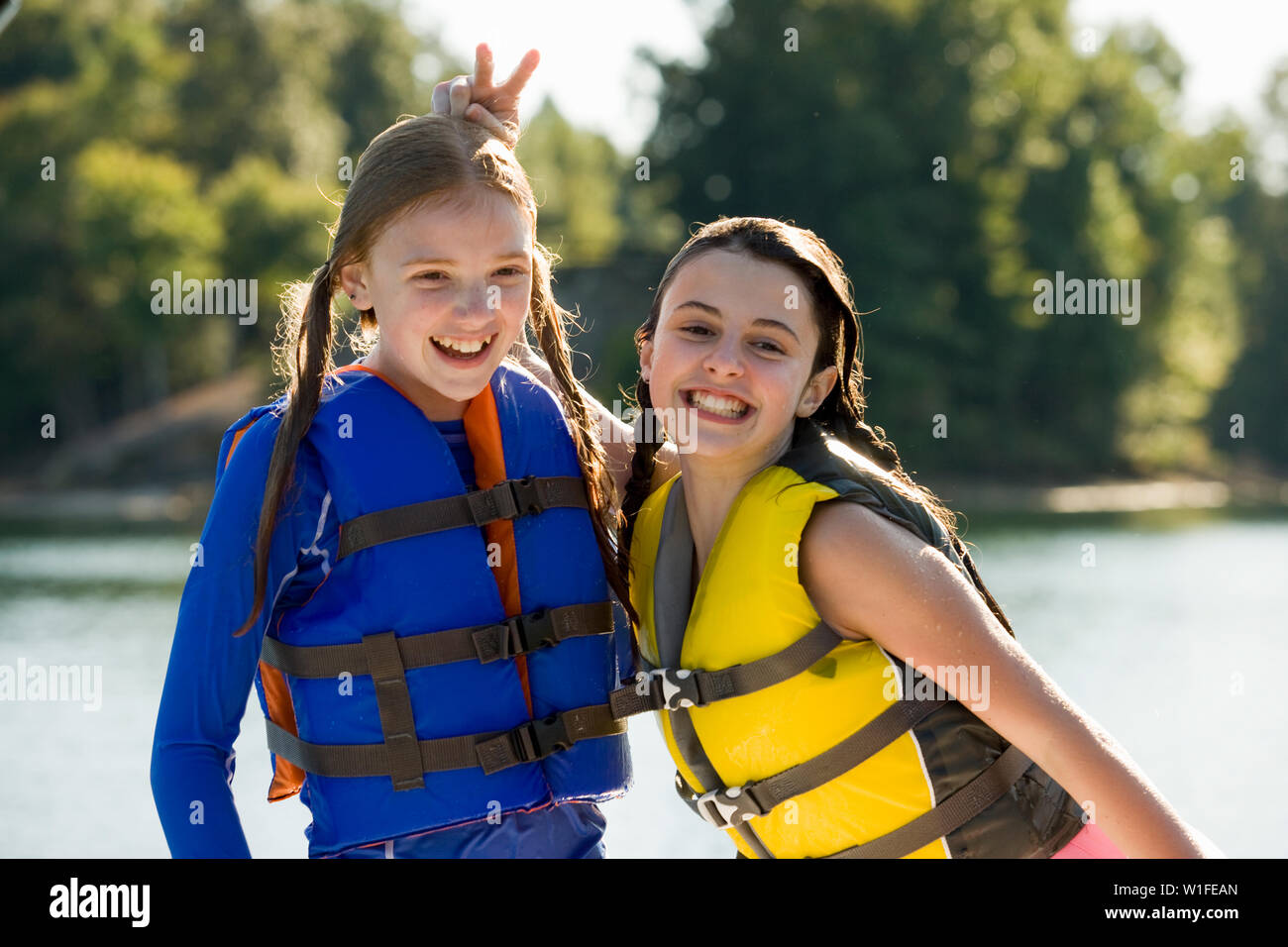 Two girls having fun wearing life jackets by a lake Stock Photo - Alamy