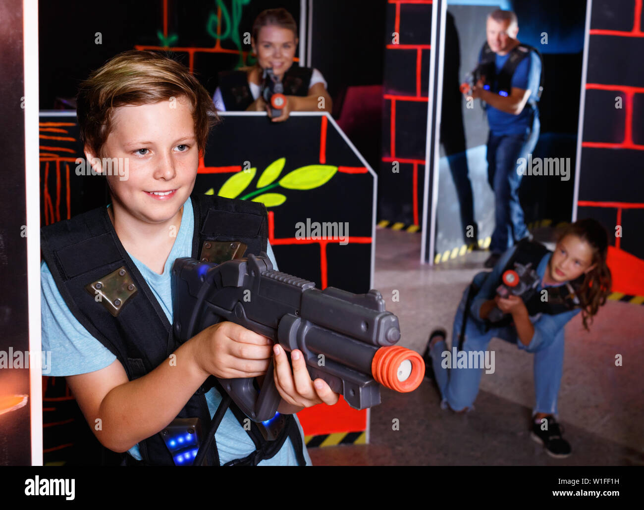 Excited cheerful positive smiling boy aiming laser gun at other players ...