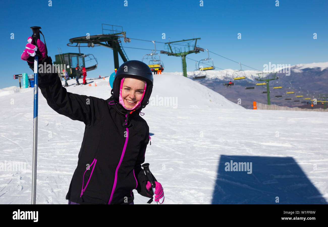 Portrait of excited smiling young woman standing with ski equipment and ...