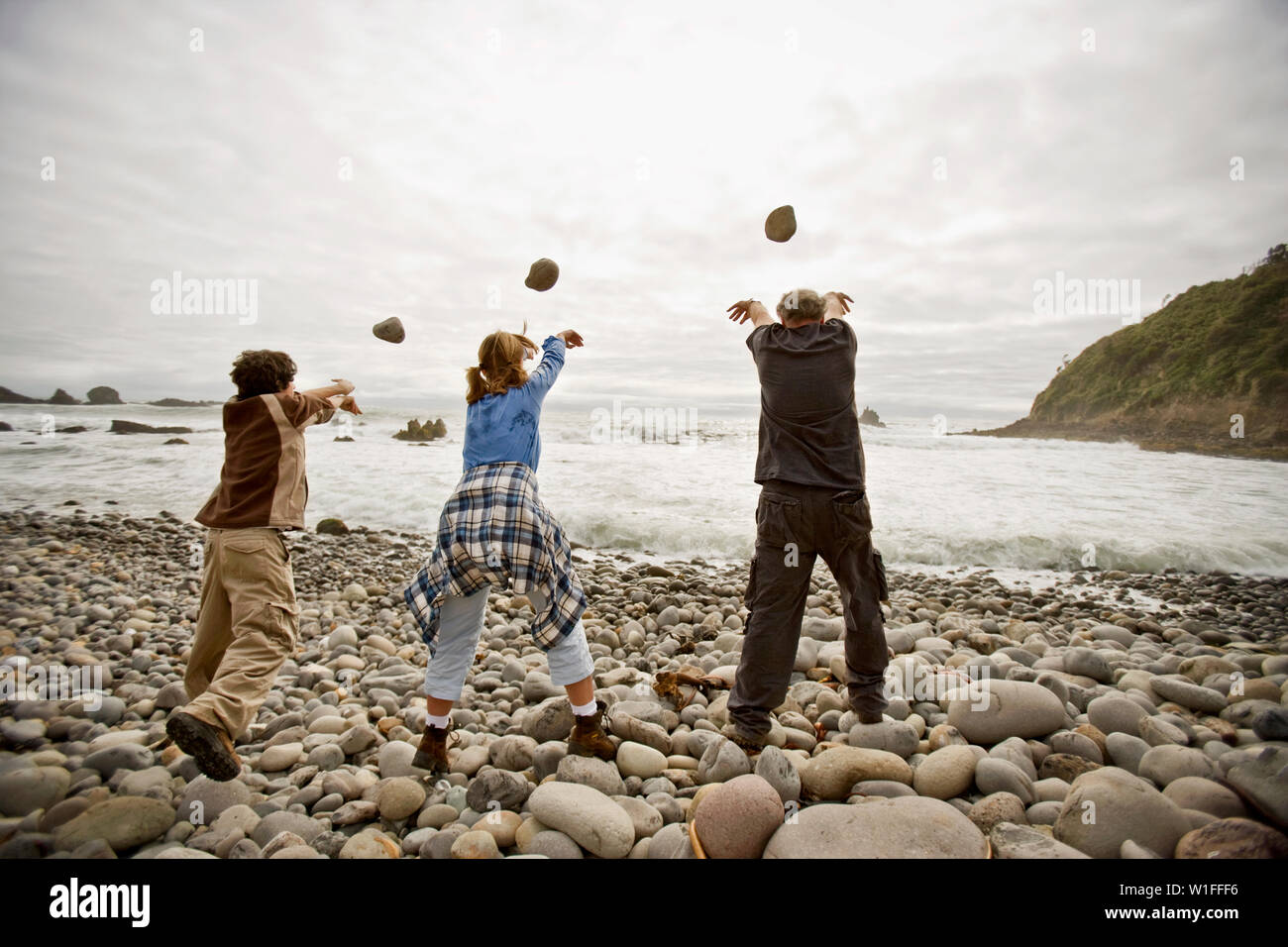 Mature man with his teenage grandchildren throwing rocks into the sea ...