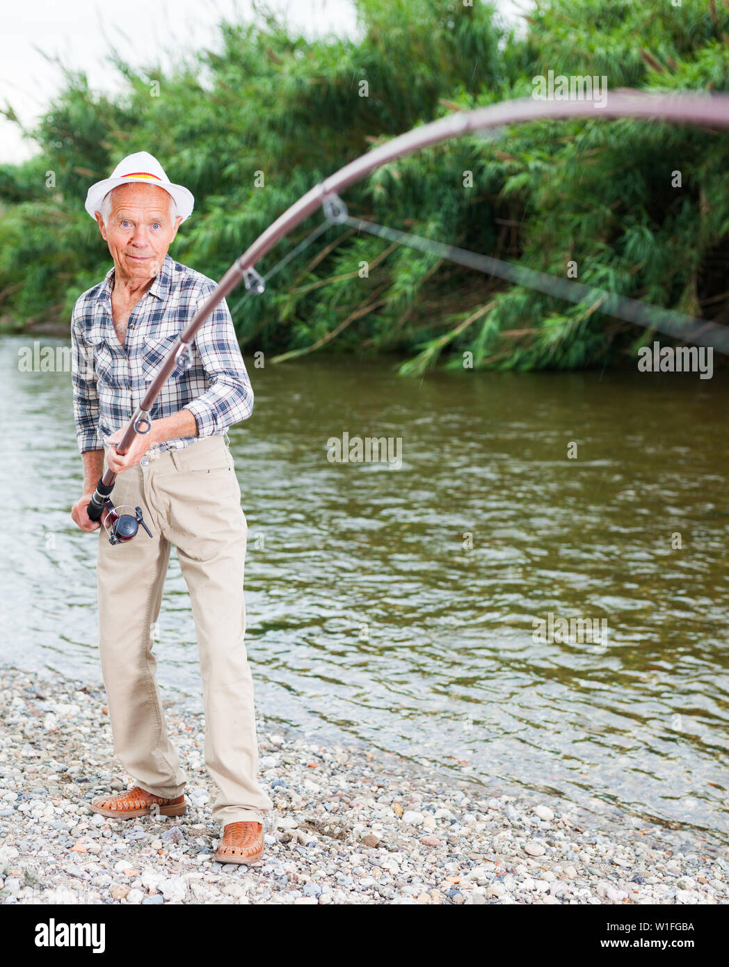 Portrait of glad aged fisherman with angling gear stretched by catch ...