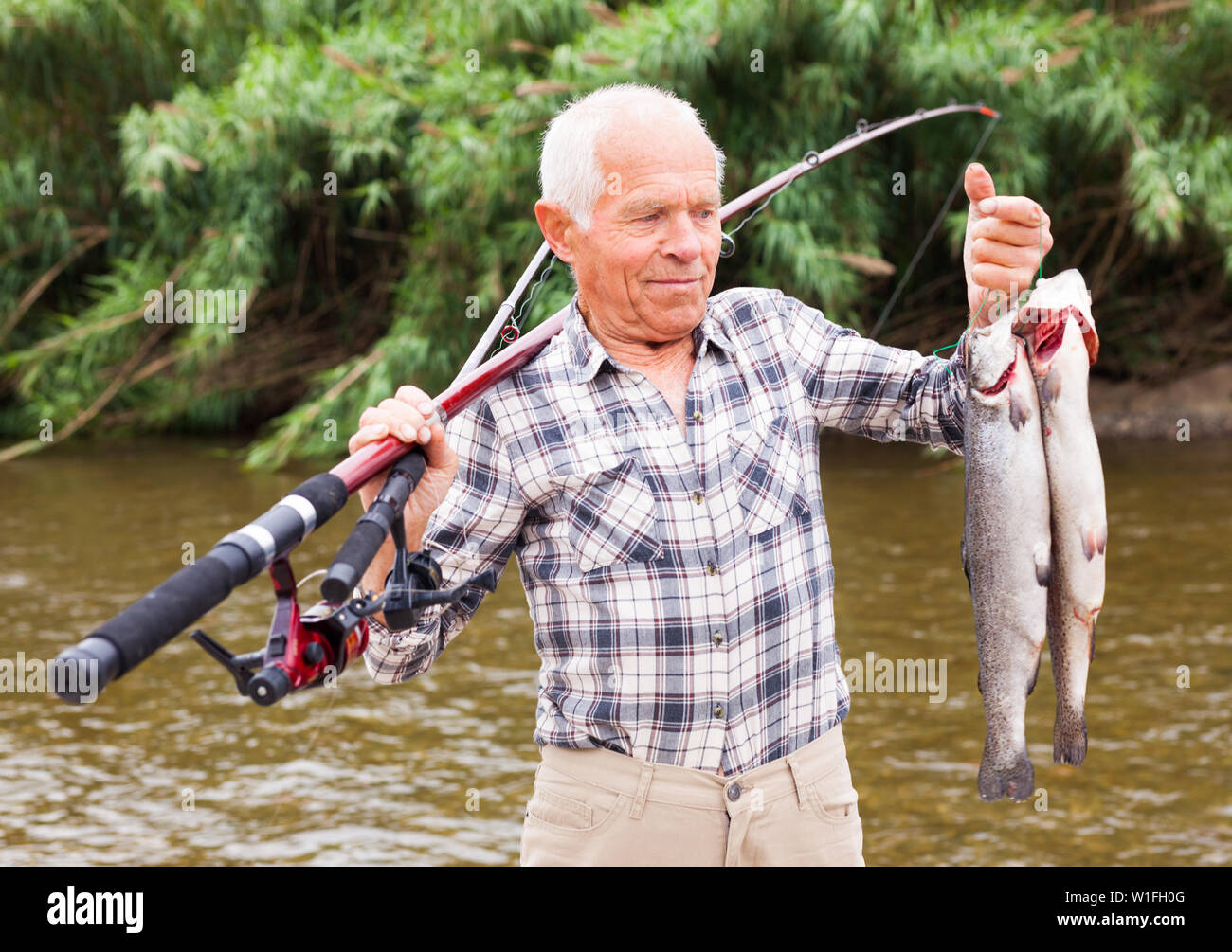 Portrait of satisfied aged fisherman with fresh catch trout at ...
