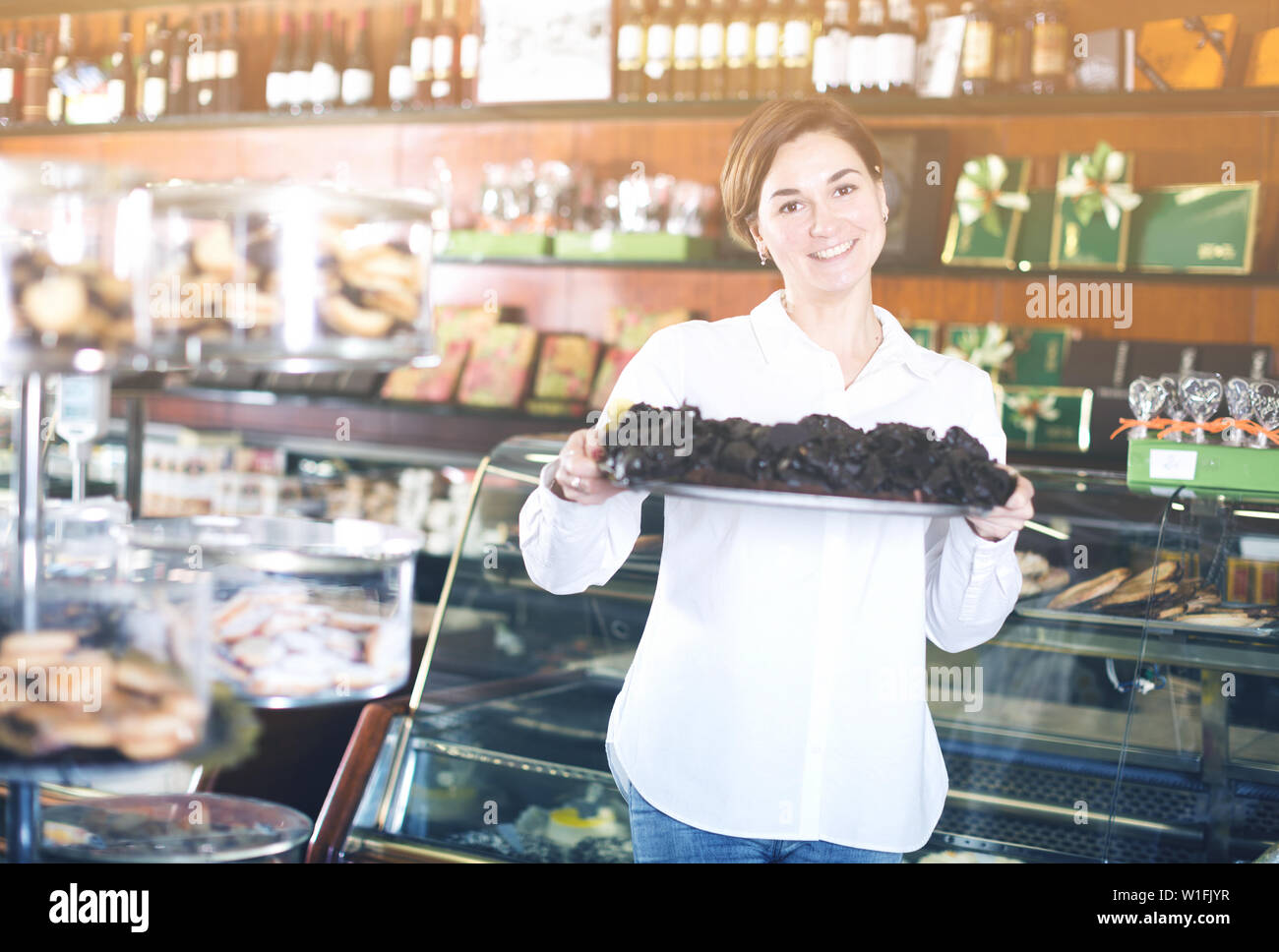 Female shop assistant demonstrating delicious cakes on tray in ...