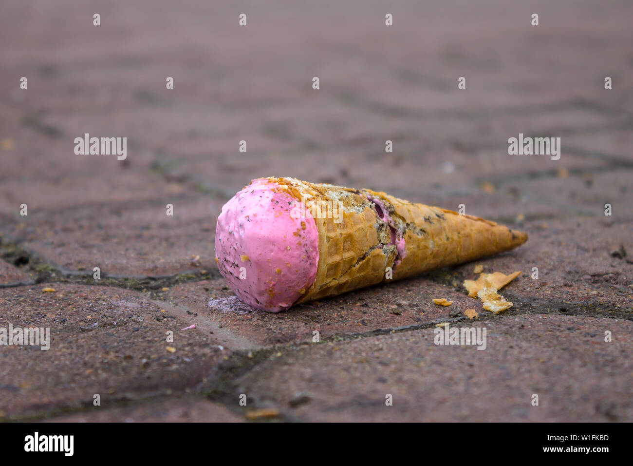 Strawberry ice cream falling on a street sidewalk and a broken waffle ...