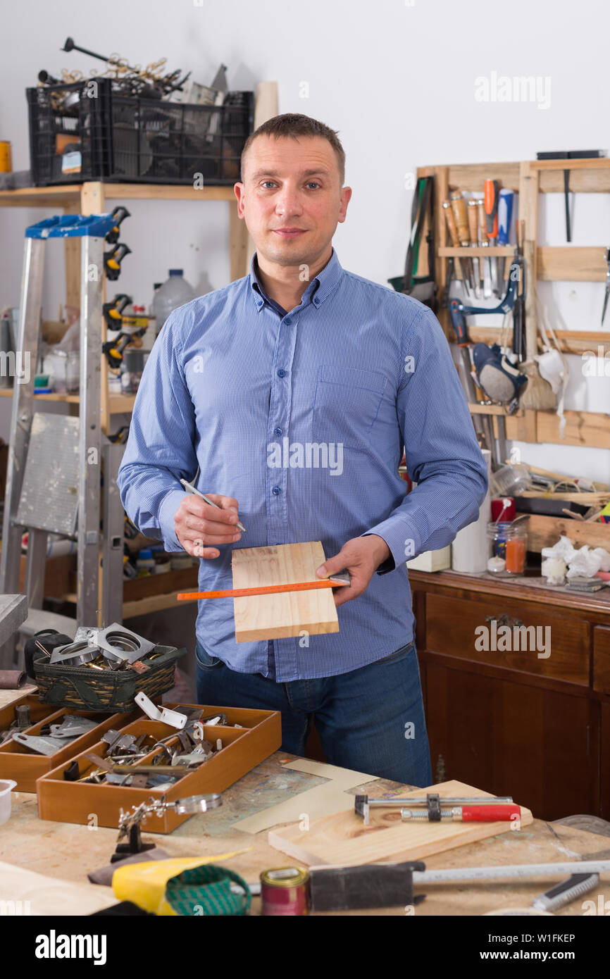 positive young russian male carpenter working wood plank at workshop ...