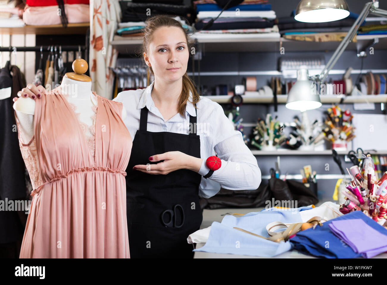 Female sewer standing near mannequin with dress at sewing workshop ...
