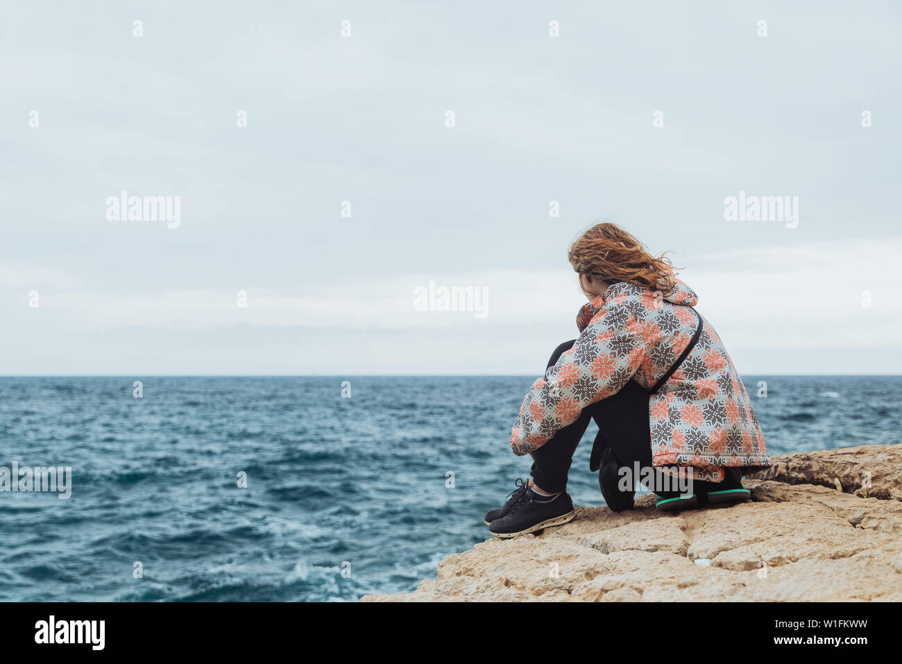woman sitting on the cliff with sad view looking at storming sea ...