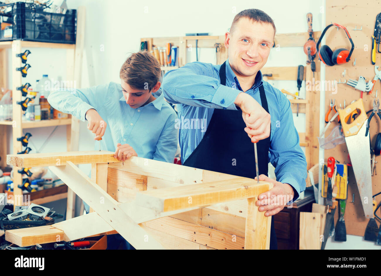 smiling teacher and boy chiselling a wooden bench in workshop Stock ...