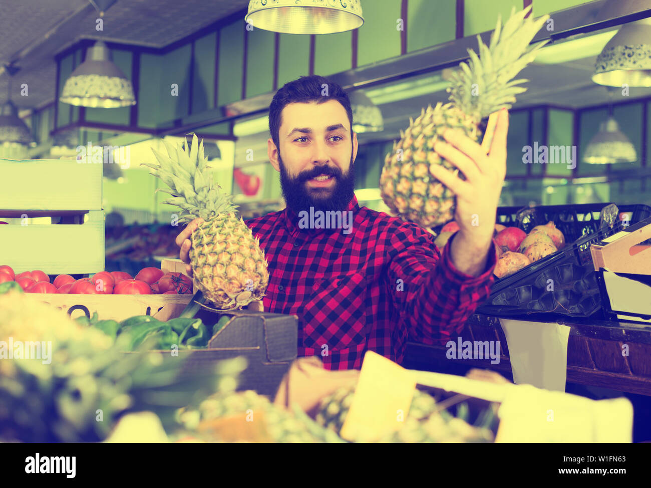 Positive Male Shop Assistant Demonstrating Pineapples In Grocery Shop