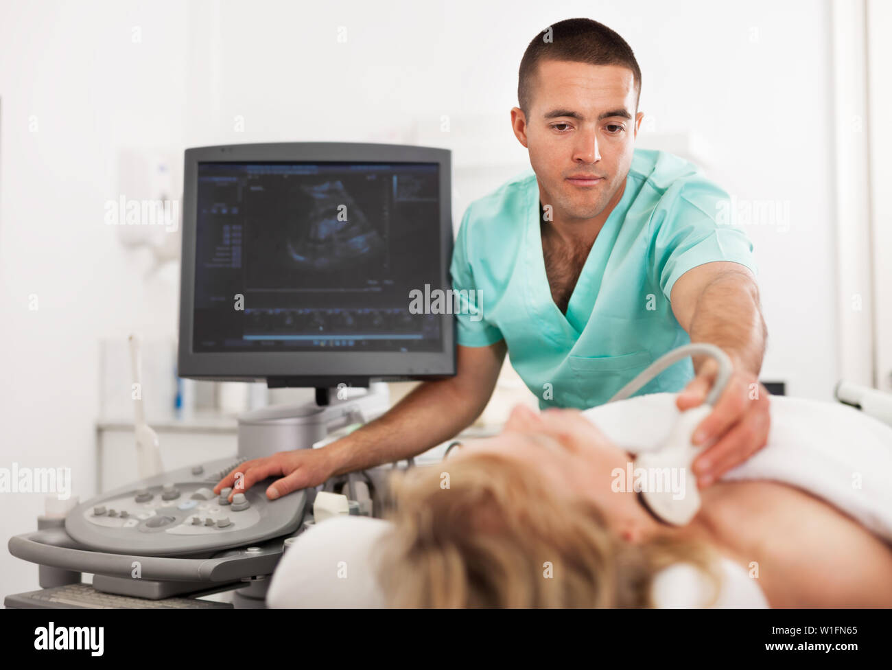 Young male doctor using ultrasound scan examining female patient at a ...