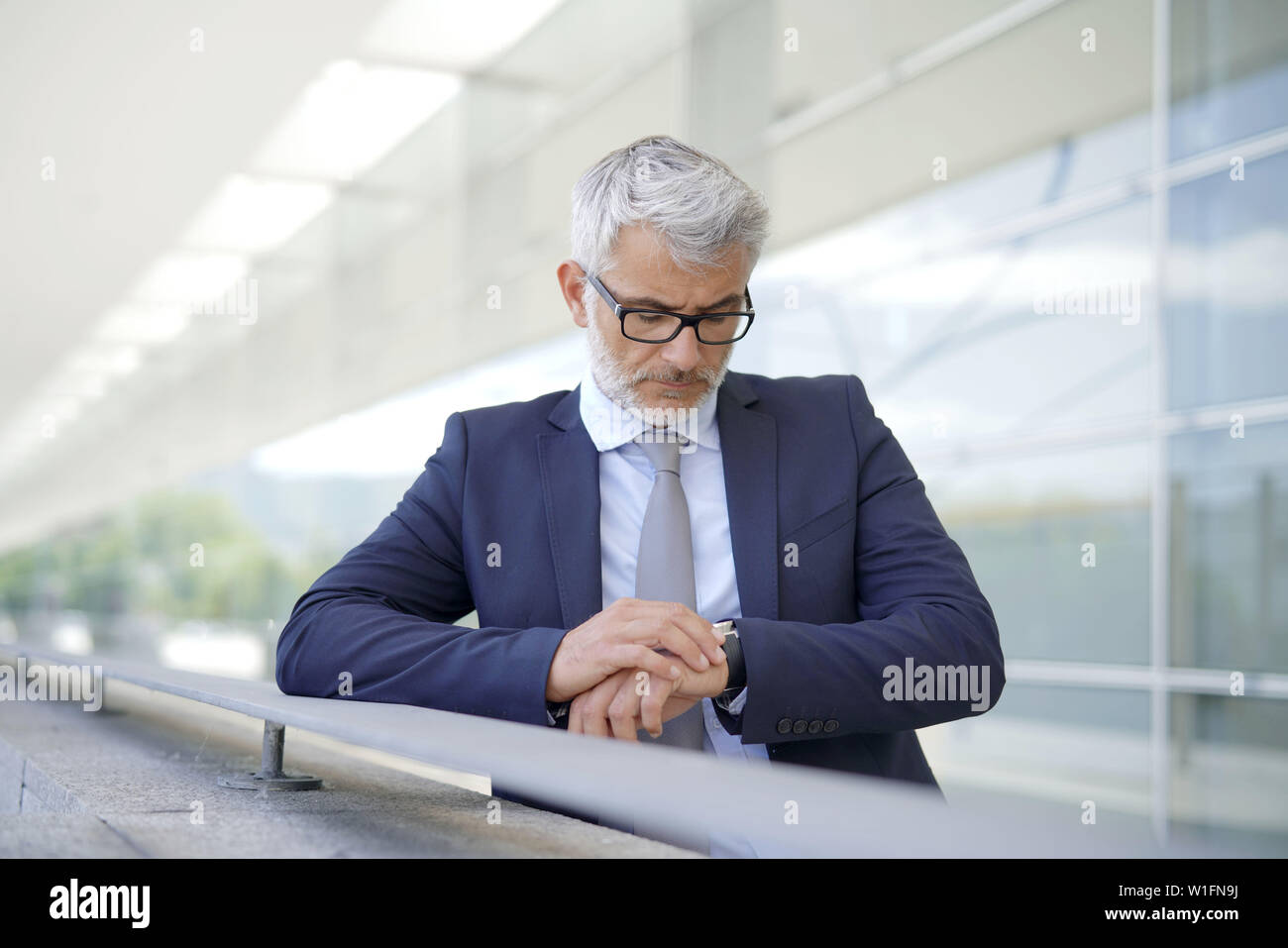 Mature businessman checking watch outside modern building Stock Photo ...