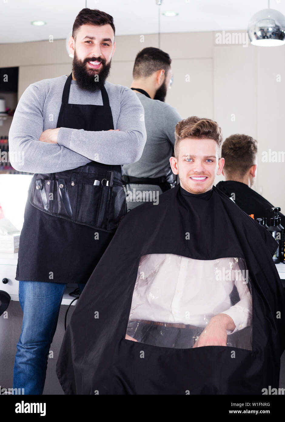Smiling adult man hairdresser demonstrating his workplace and tools at ...