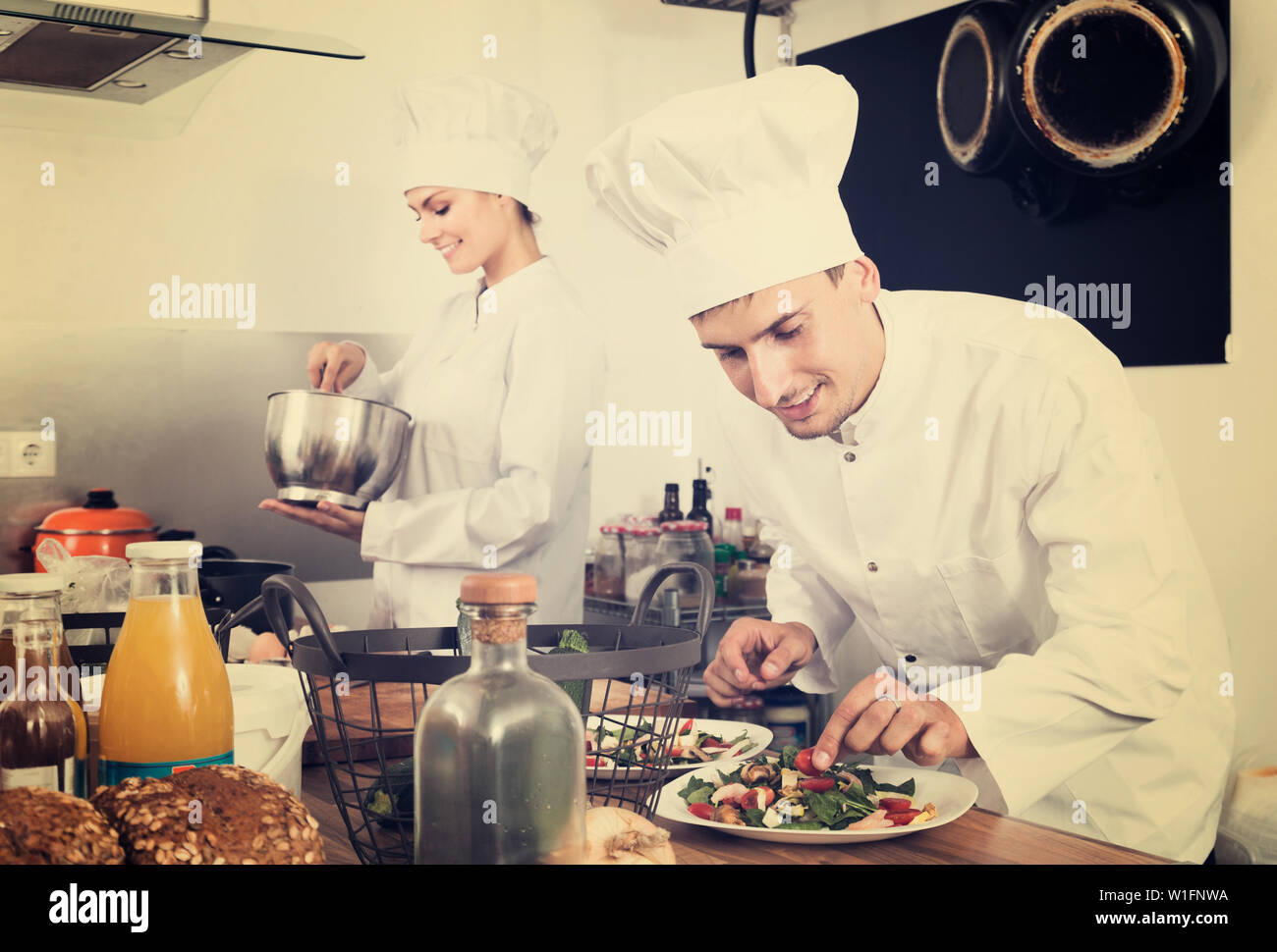 Two young man and woman chefs cooking food at restaurant's kitchen ...