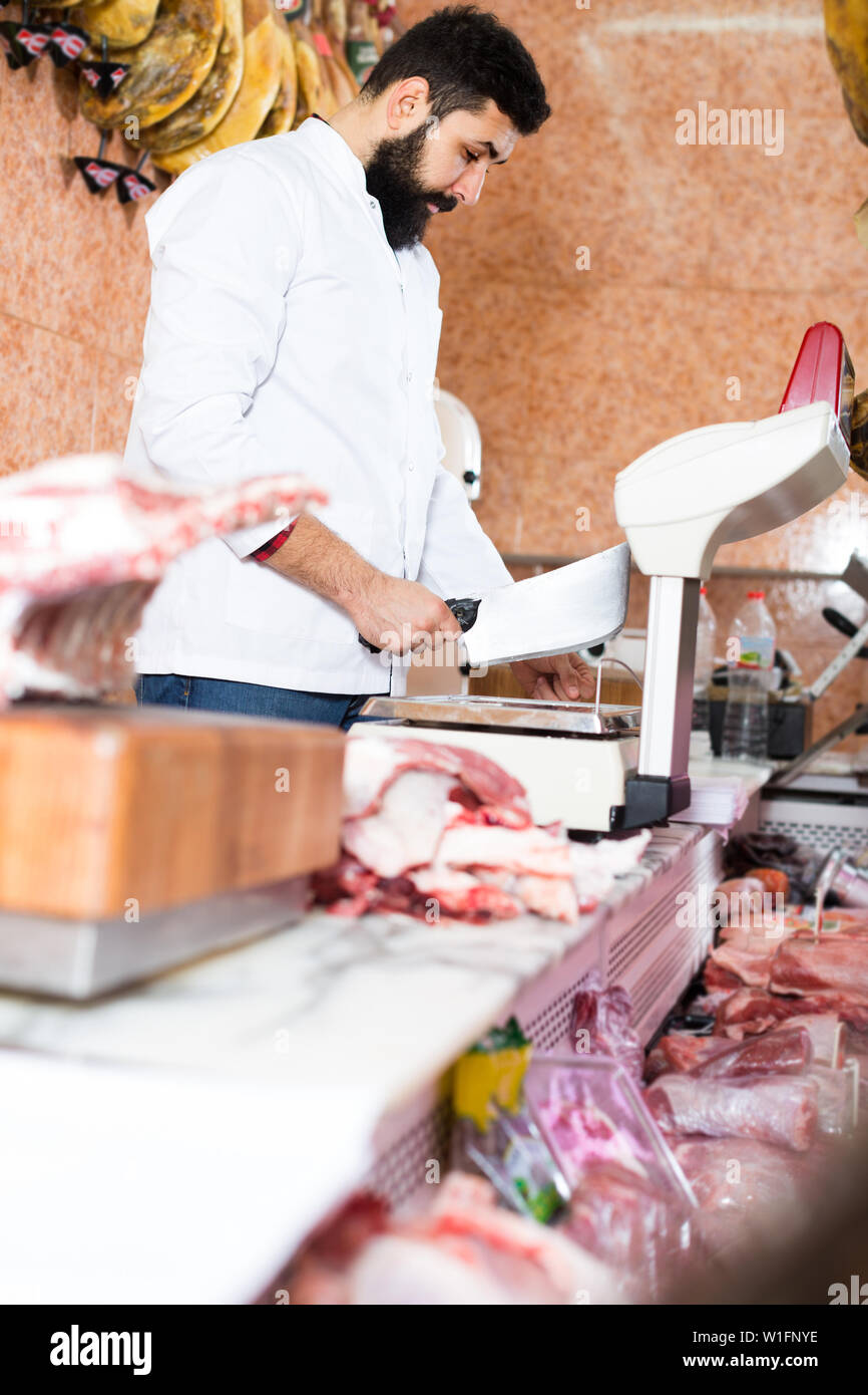 Male shop assistant 20s carving meat to sell in butcher’s shop Stock ...