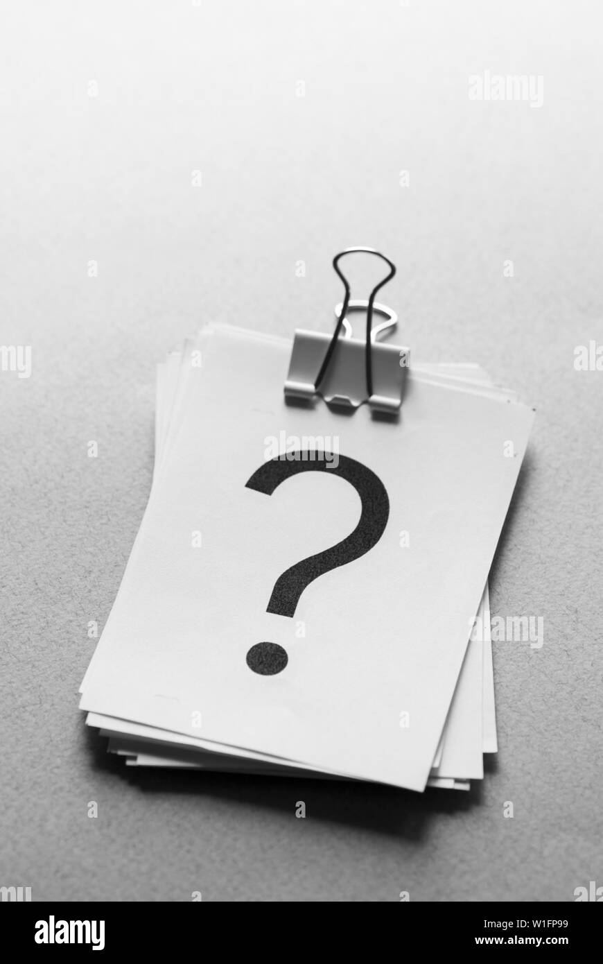 Stack of white cards printed with question marks held together with a ...