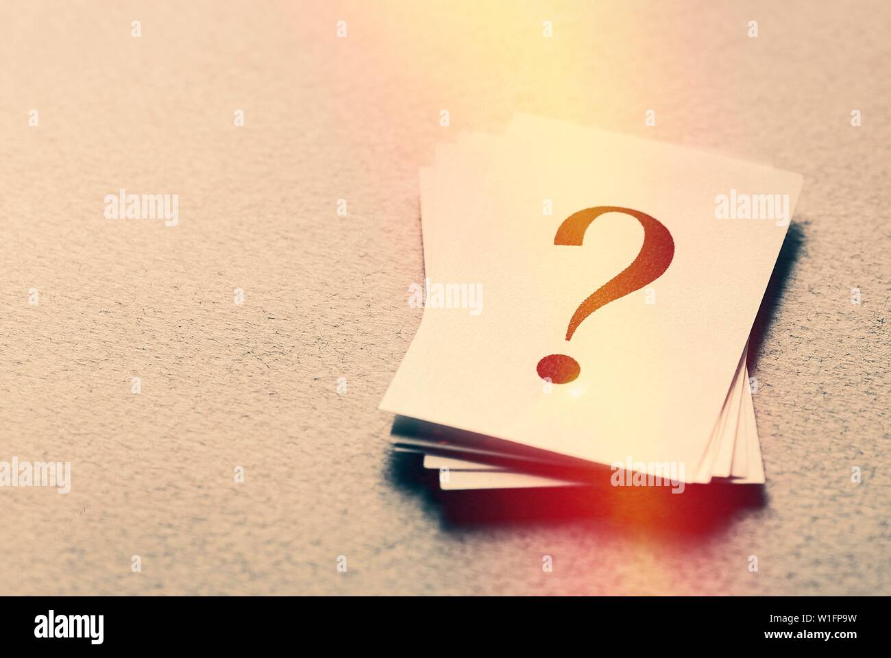 Pile of cards with printed question marks on a textured grey surface ...