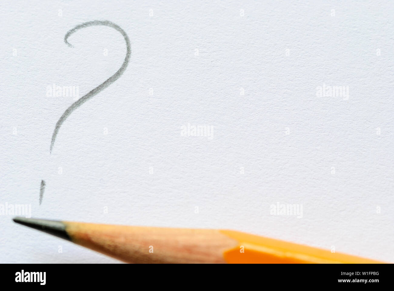 Sharp pencil lying next to question mark on white paper with copy space ...